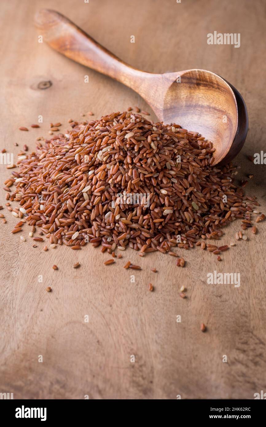 pile of whole grain dark brown rice with a wooden spoon, also called ...