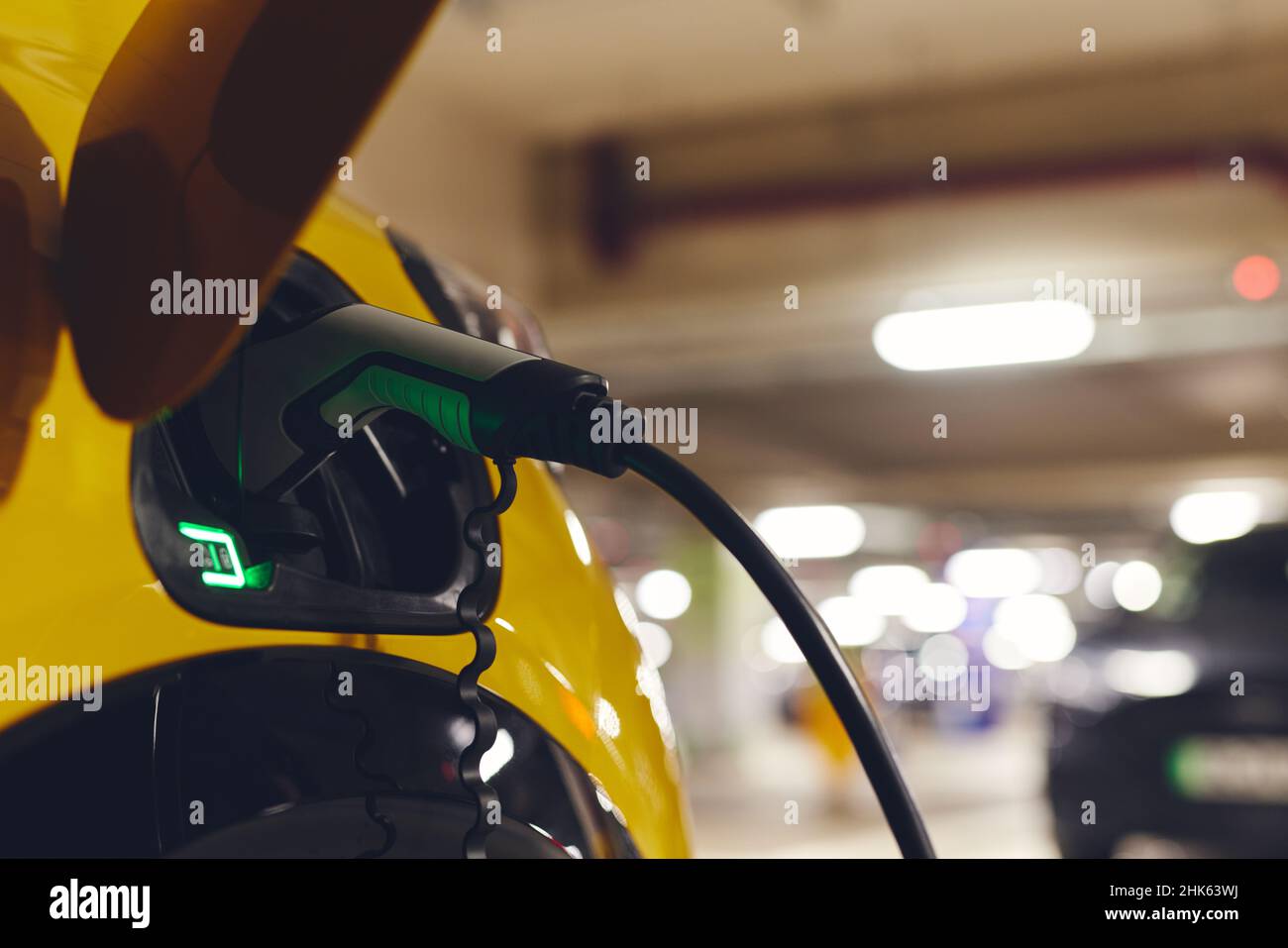 Plugged in electric car charging in mall car park with green charging ...