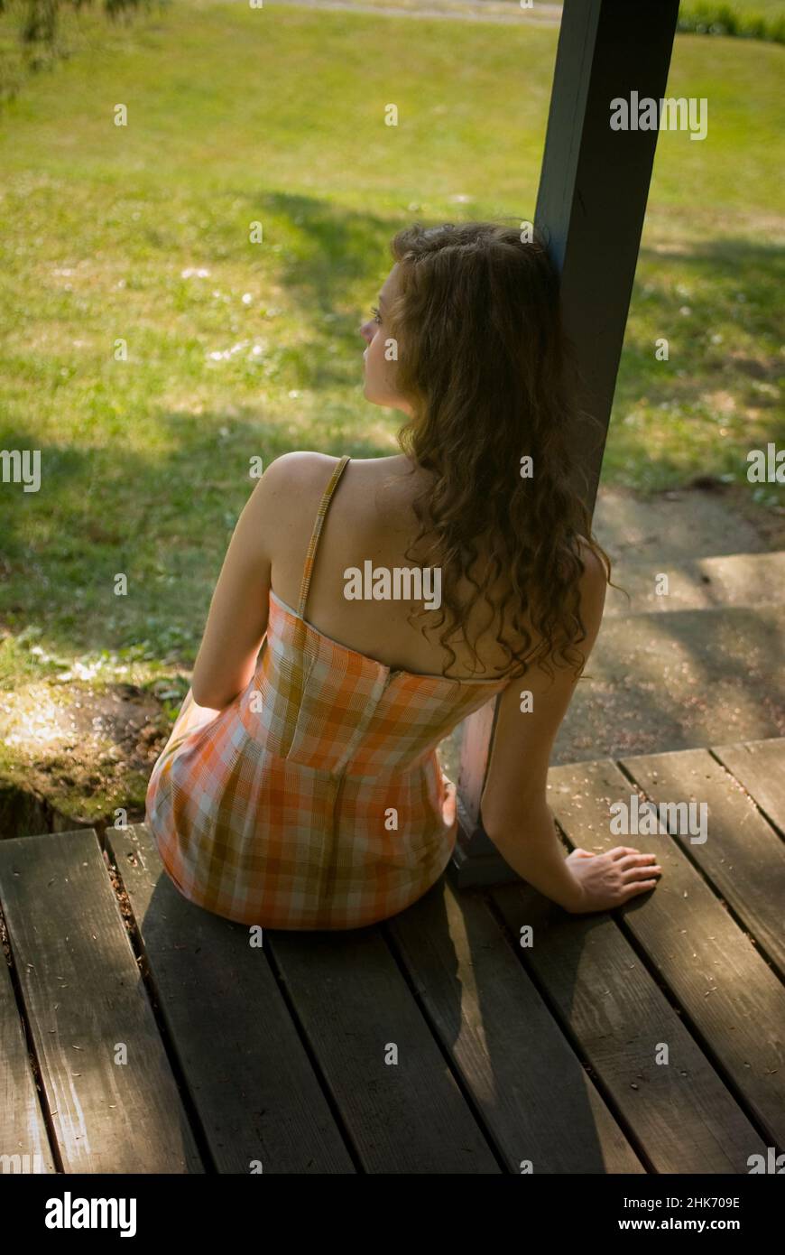 Rear view of young woman sitting on porch leaning on column Stock Photo ...