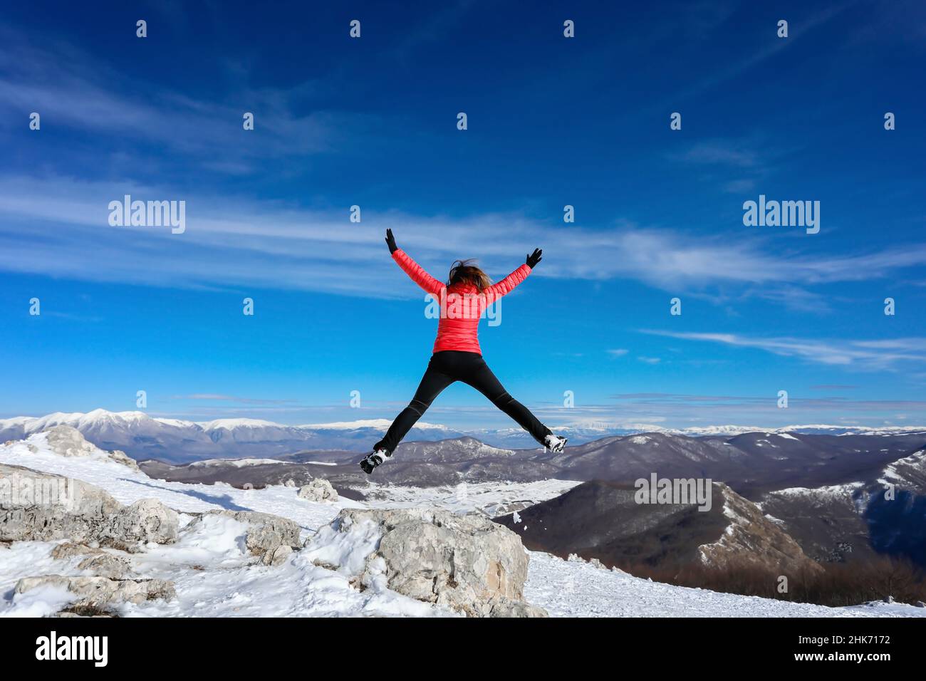 Hiker on top of the mountain happily jumps into the blue sky in front ...