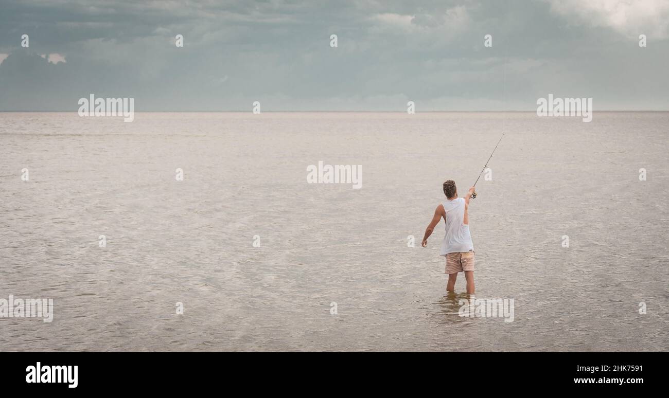 Back view of a man fishing in the shallow water Stock Photo - Alamy