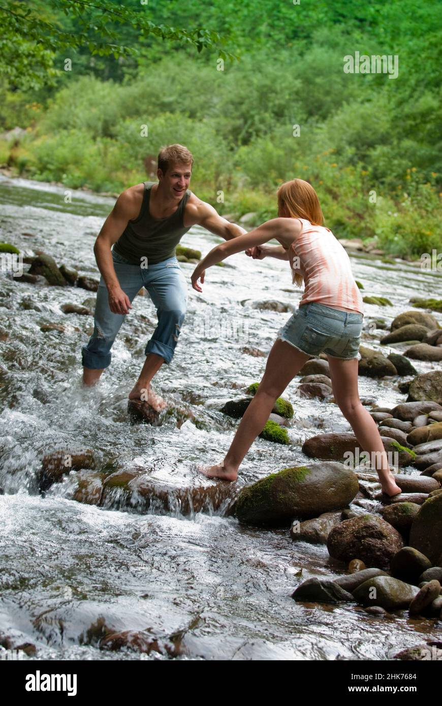 Young couple helping each other over a stream Stock Photo - Alamy