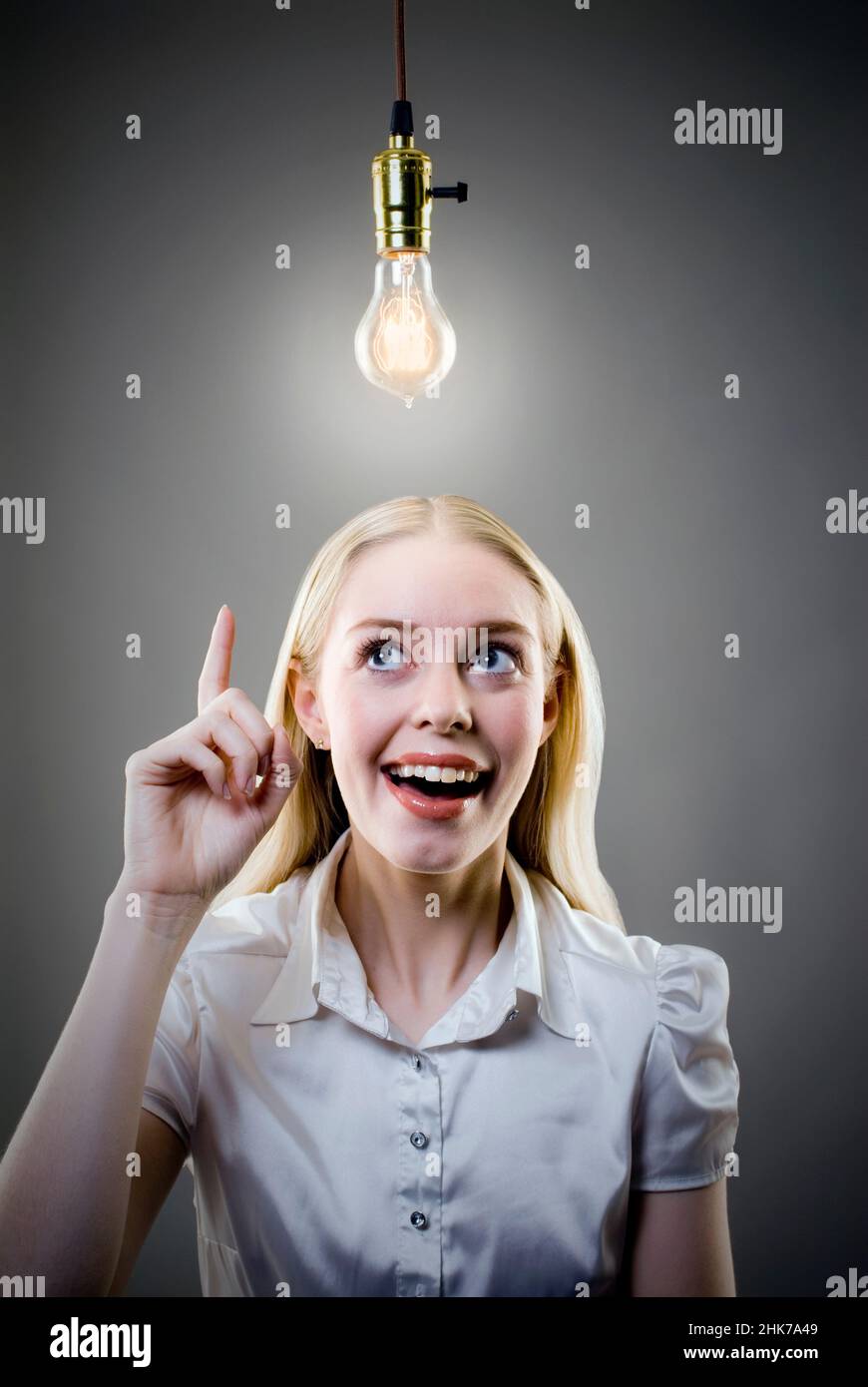 Young blonde woman, finger pointing up at lit Edison light bulb Stock ...