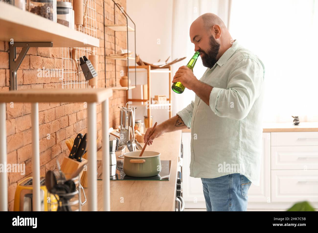 Bald man drinking beer while cooking in kitchen Stock Photo - Alamy