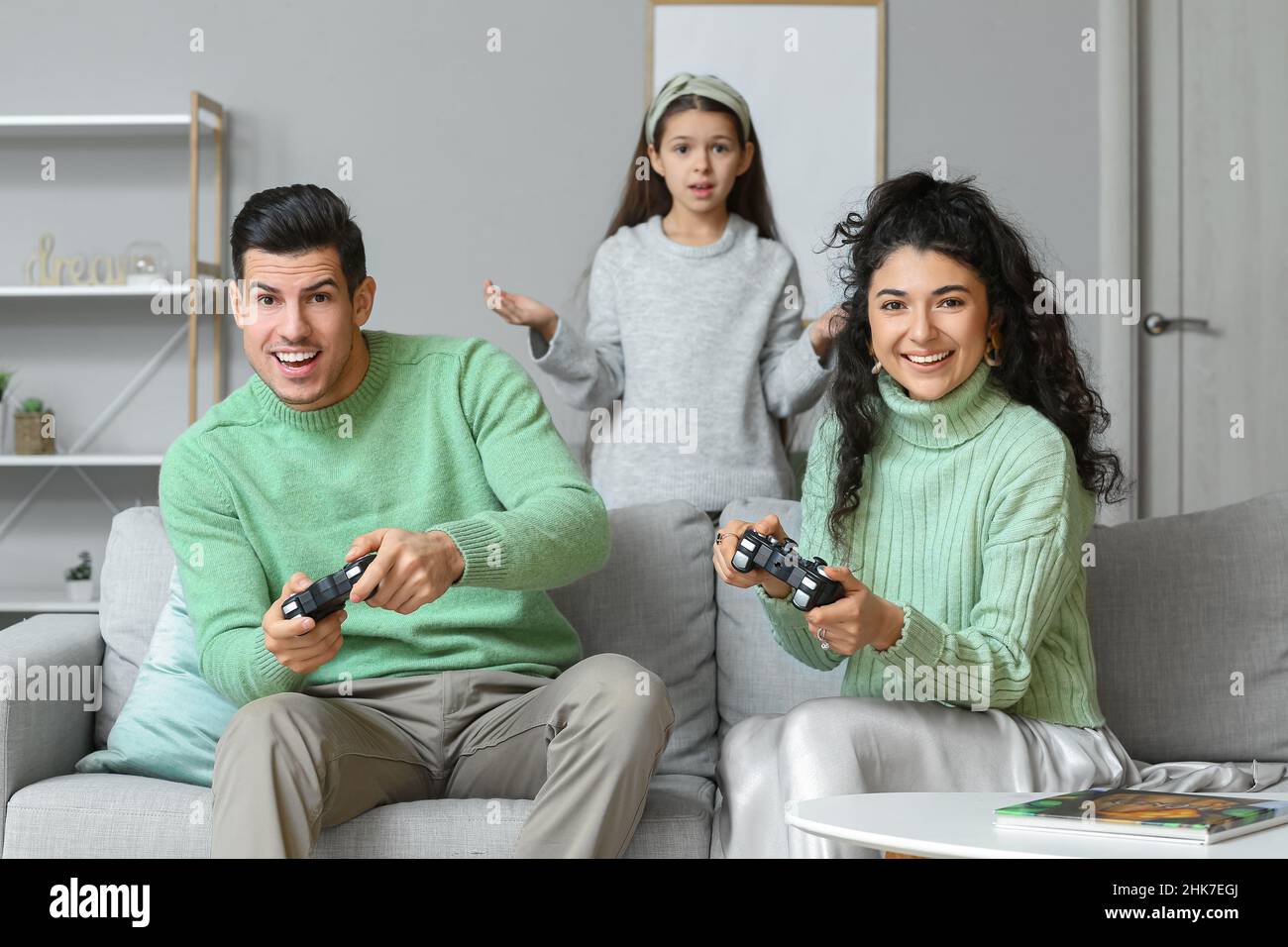 Confused little daughter and her parents in warm sweaters playing video ...