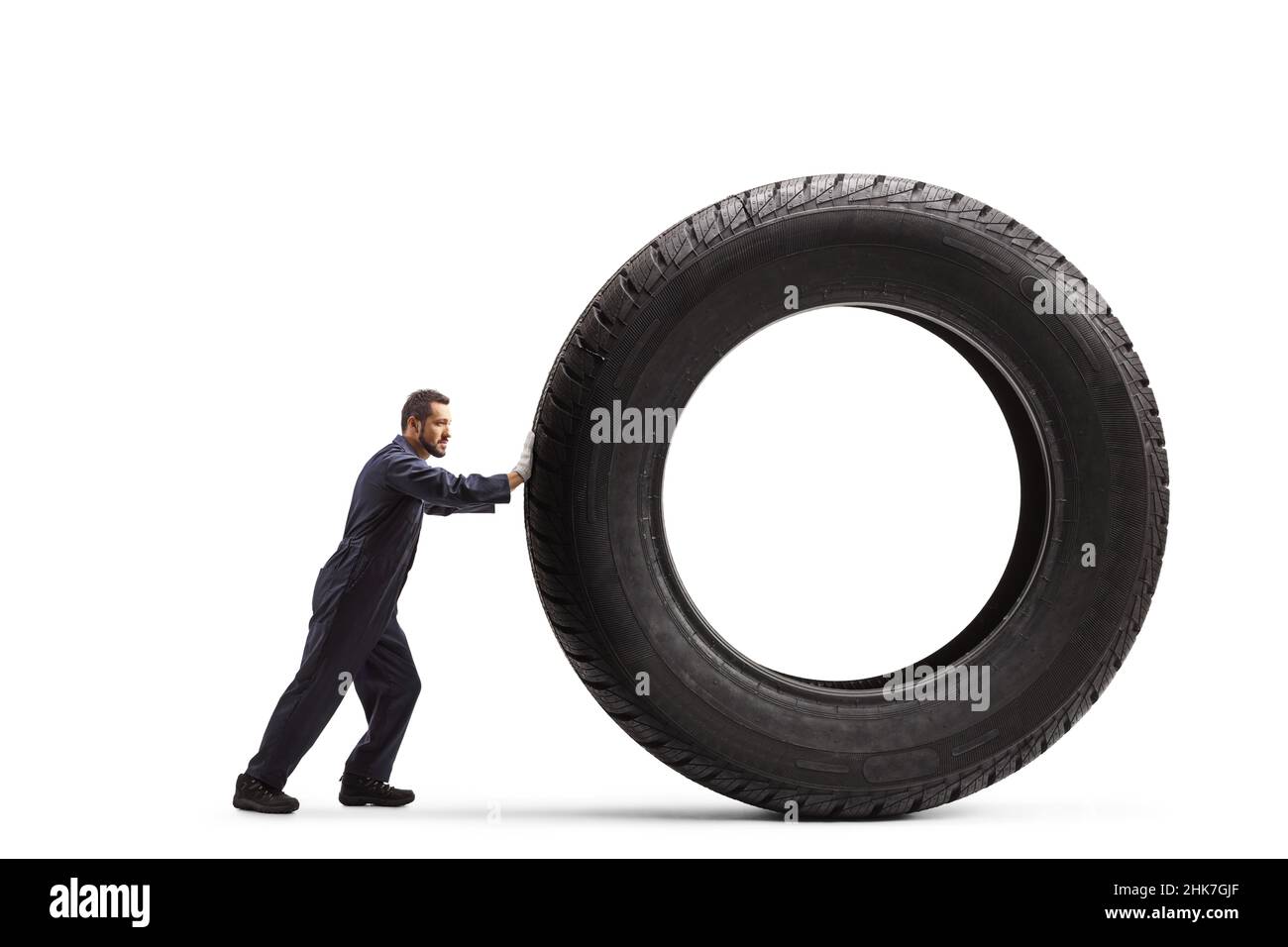 Full length profile shot of a mechanic pushing a big vehicle tire ...
