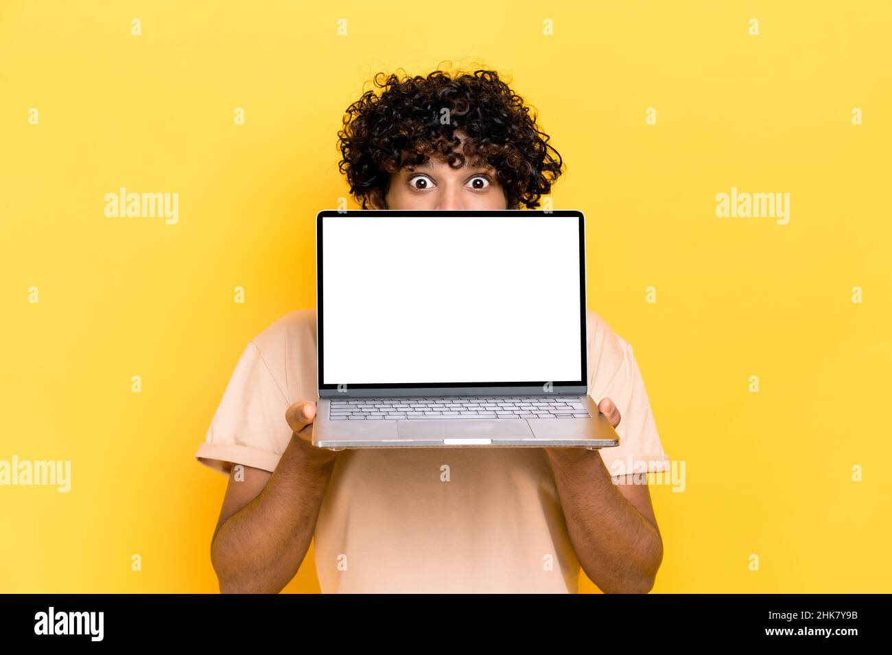 Shocked indian guy, peeking out from behind laptop, looks surprised at ...