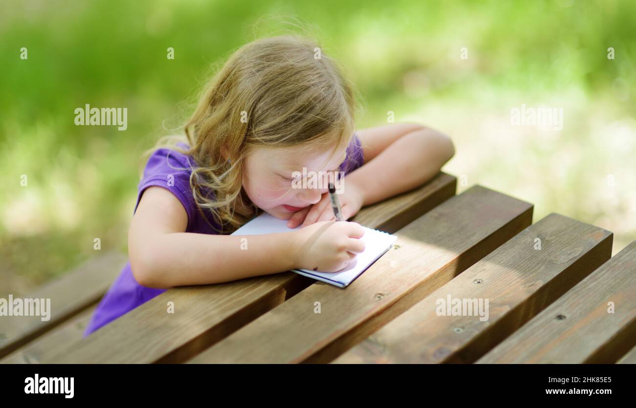 Little girl drawing at the wooden table outdoors. Little kid sketching ...