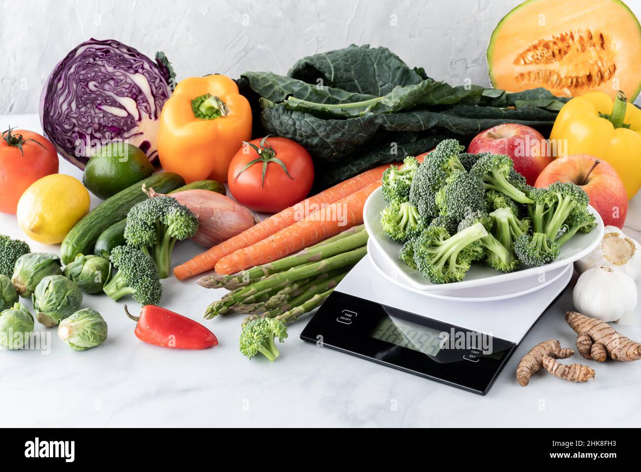 A dish full of broccoli on a food scale with a variety of produce in ...