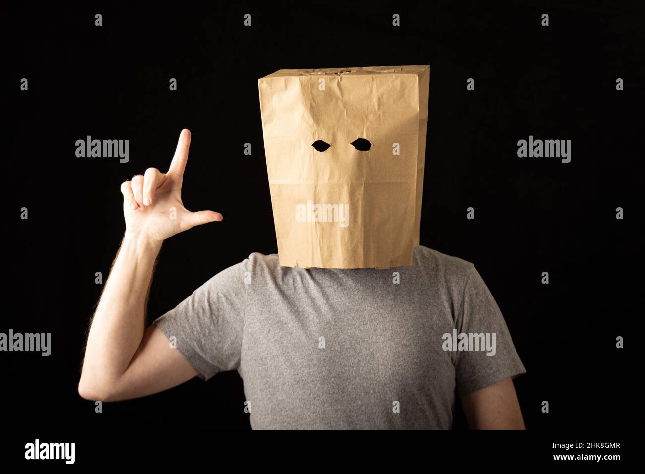 Man wearing a brown paper bag over his head and making a loser symbol ...