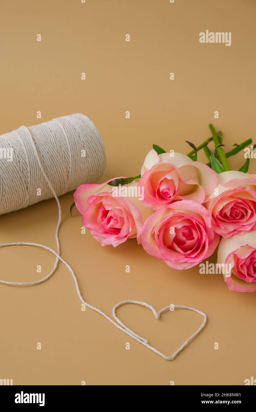 Delicate pink roses with spool of white cotton rope in heart shape on ...