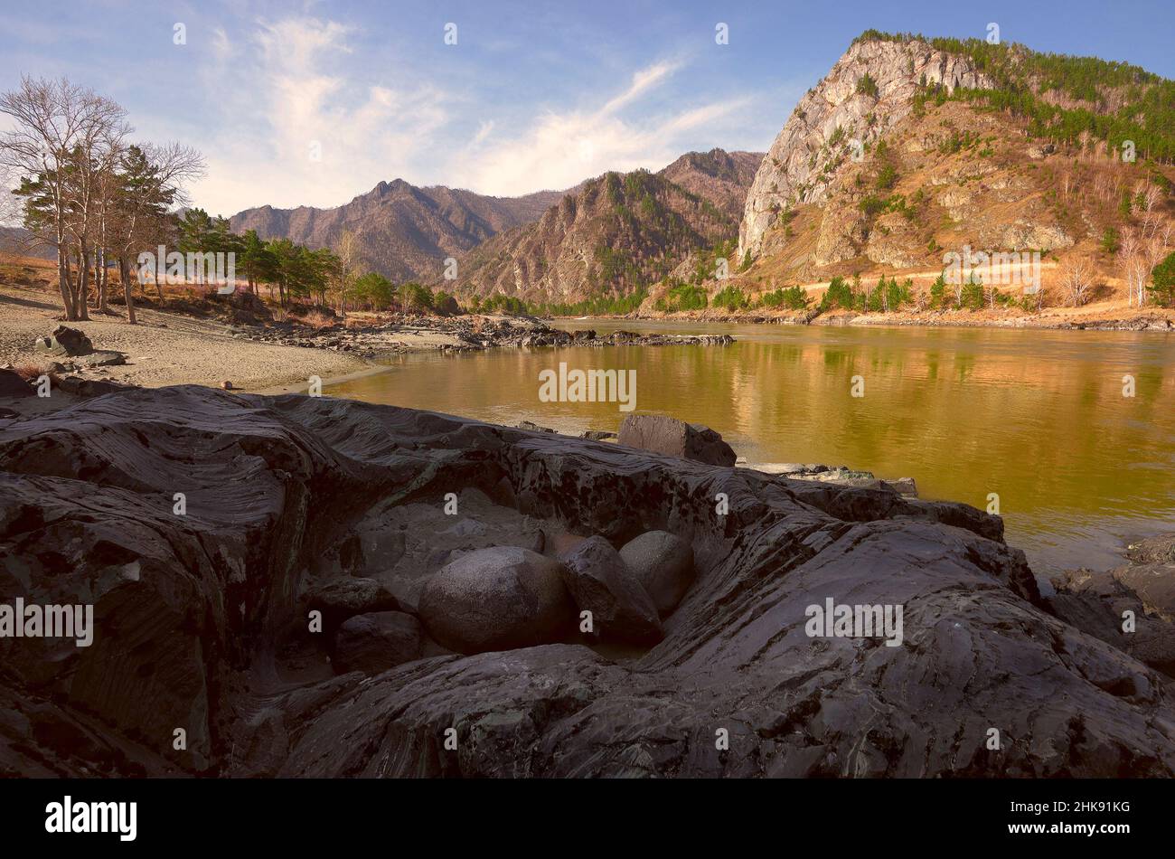 Wavy layered black rocks on the Bank of a mountain river. Round egg ...
