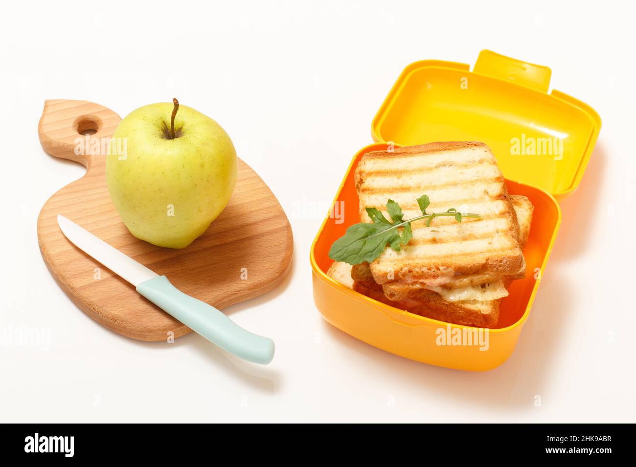 Yellow lunch box with toasted slices of bread, cheese and green parsley ...