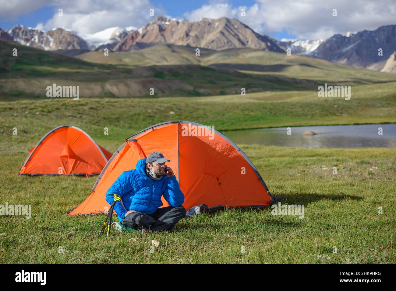 Man sitting after a mountain hike in the camp and talking by satellite ...