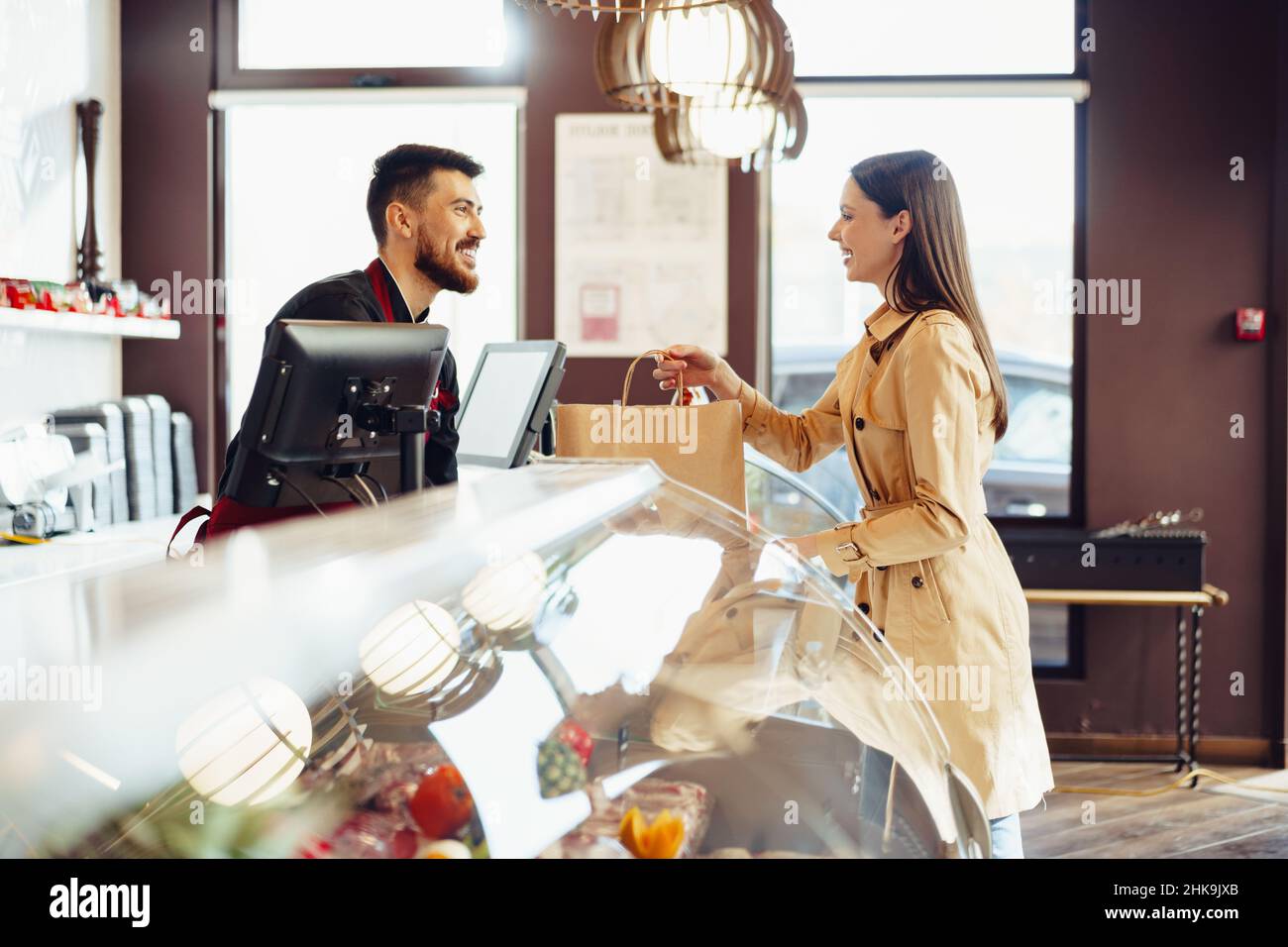 Shop assistant handling shopping bag to female customer in grocery ...