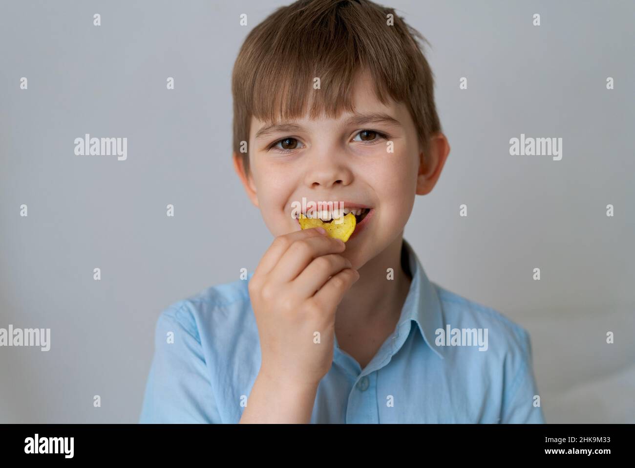Young little caucasian child eating unhealthy potato chips on a gray ...