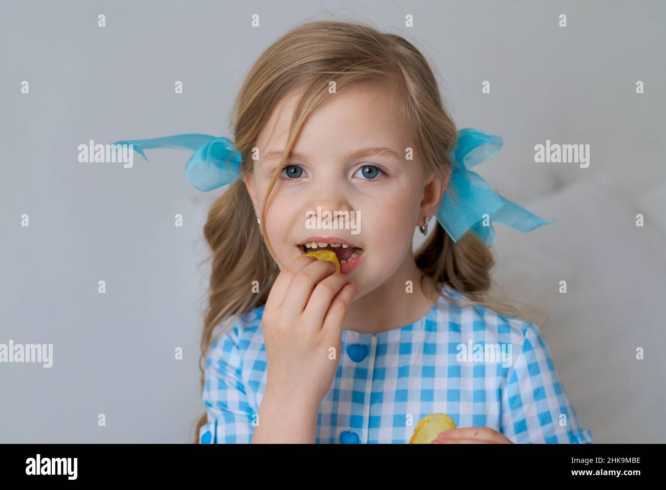 Portrait happy little caucasian girl eating crispy potato chips on gray ...