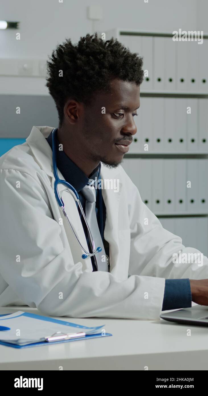 African american doctor using laptop while sitting at desk in hospital ...