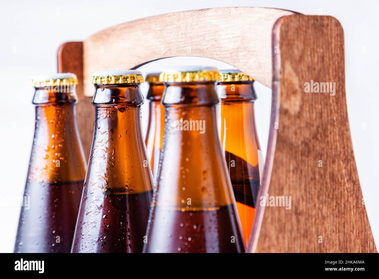 Close-up of wet six bottles necks of beer in a wooden case on a white ...