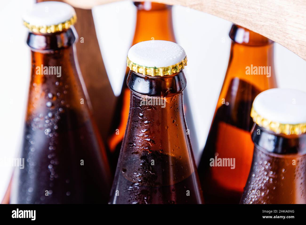 Close-up of wet six bottles necks of beer in a wooden case on a white ...