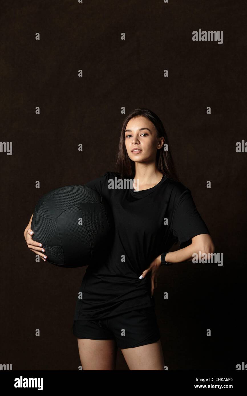 Sporty girl in special sportswear staying with big fitness ball on dark ...