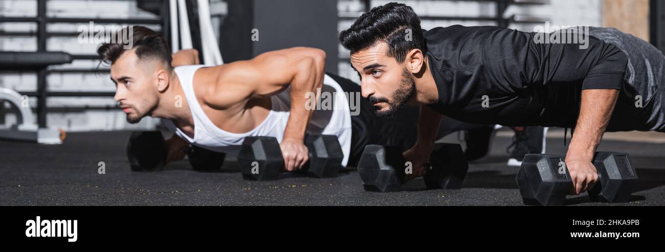 Arabian man working out with dumbbells near sportsman in gym, banner ...