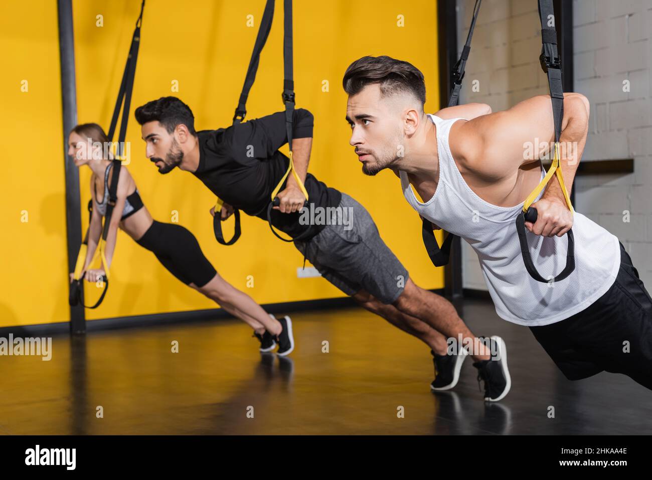 Young sportsman pulling suspension straps near blurred multiethnic ...