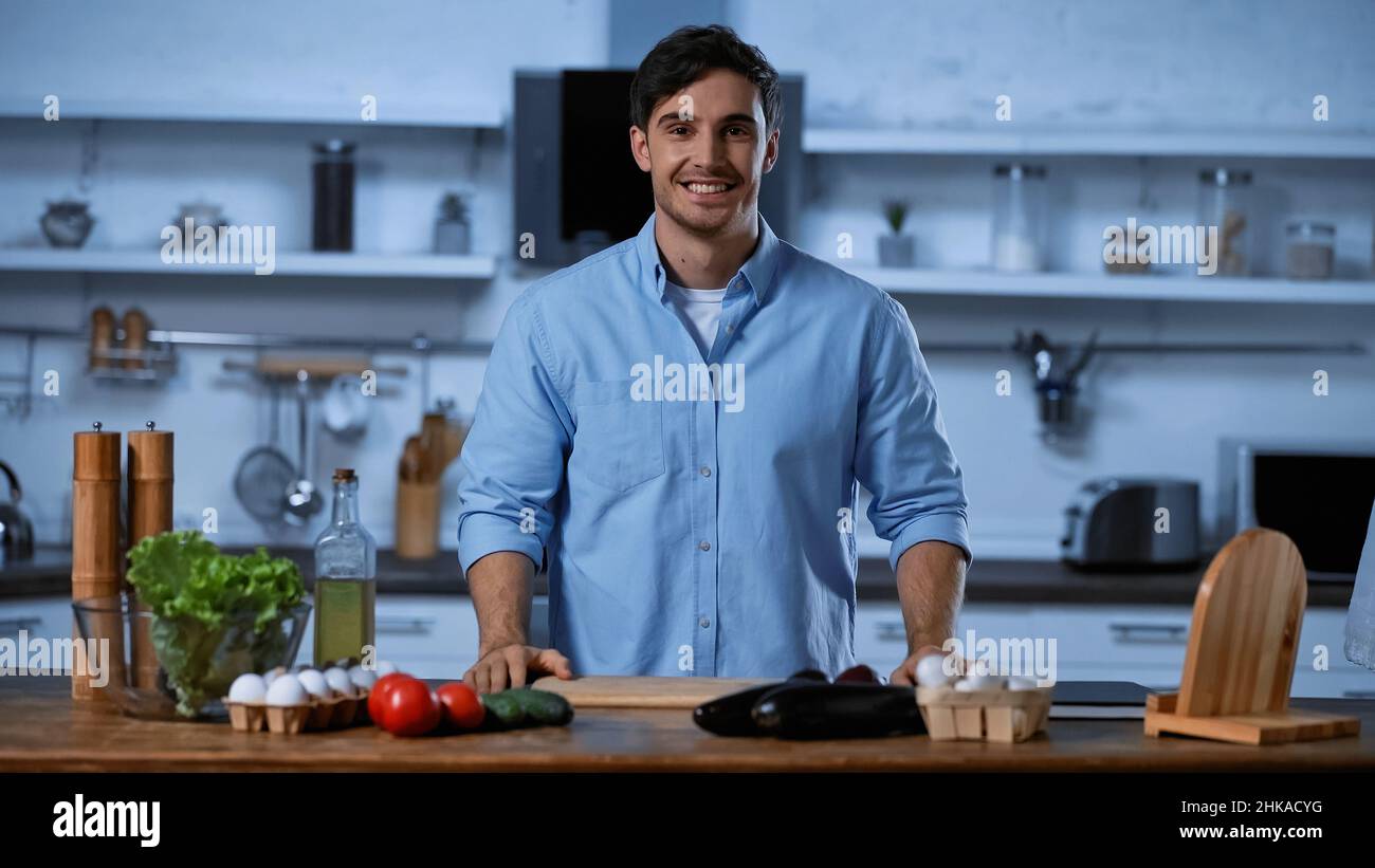 smiling man looking at camera while standing near table with fresh ...