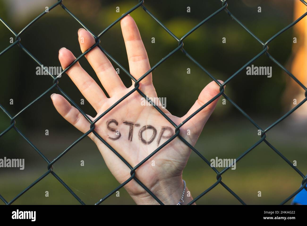 Female hand with Stop sign behind a fence. Stop - here is a border ...
