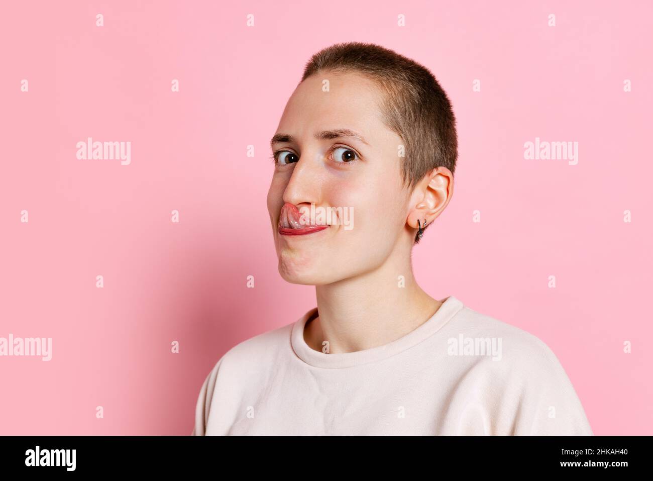 Funny young woman, student with short hair touching nose with tongue ...