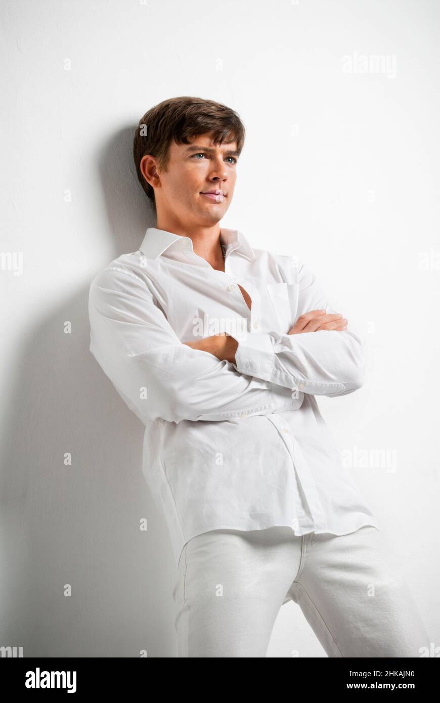 Young man leaning against white wall, arms folded Stock Photo - Alamy