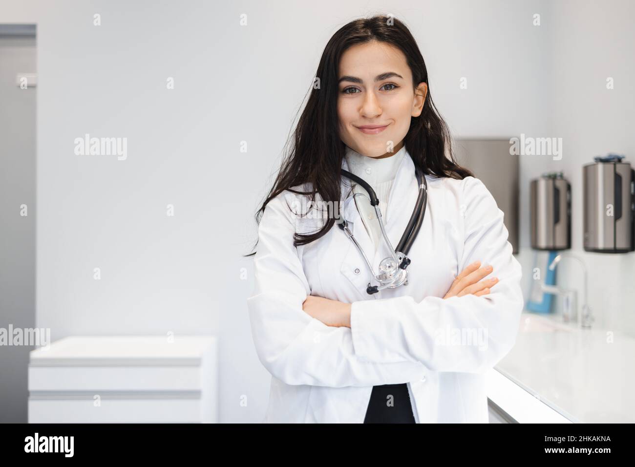Portrait of cheerful female doctor in lab coat standing with crossed ...
