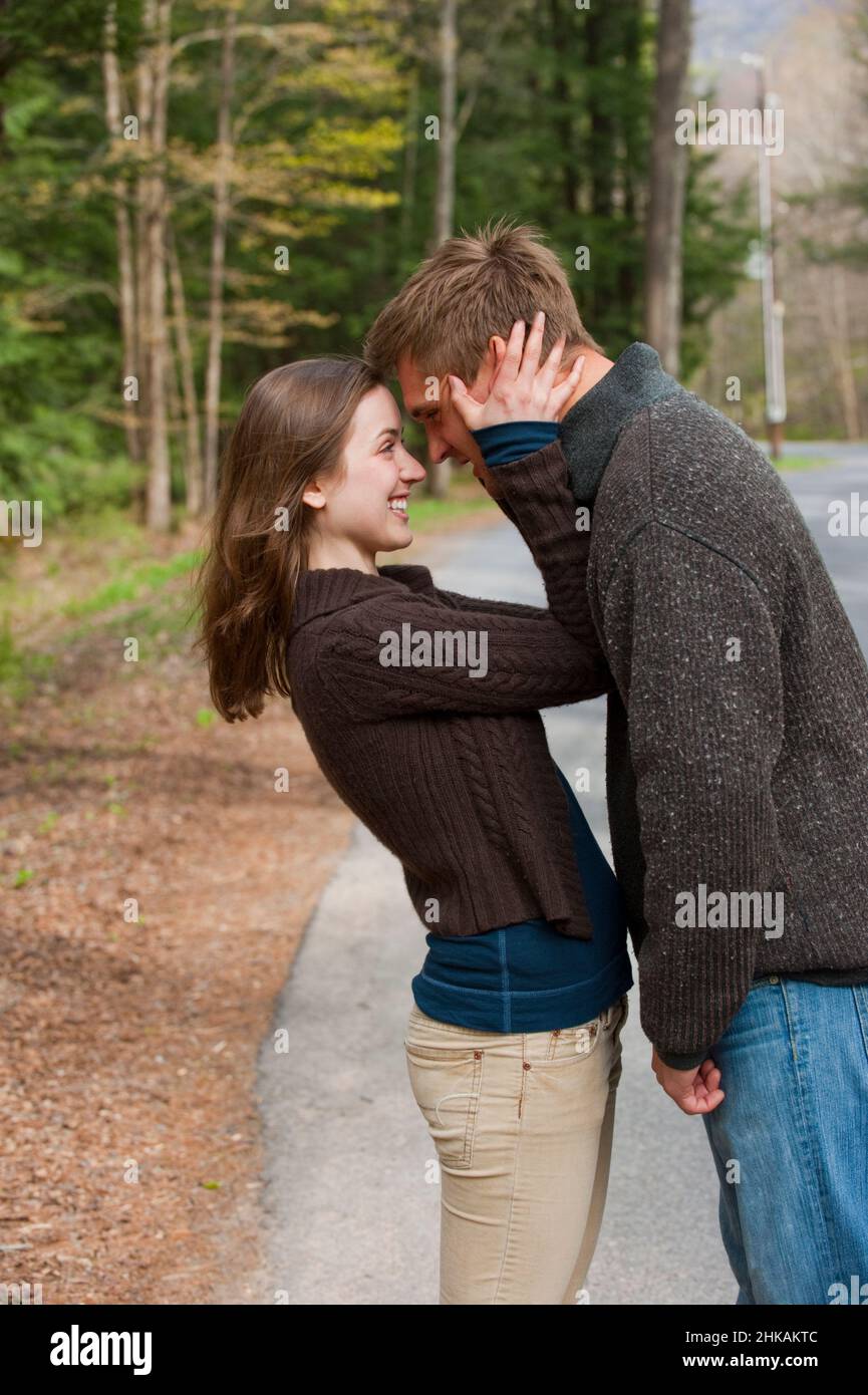Young woman reaching up and putting her hands around a young man's face ...