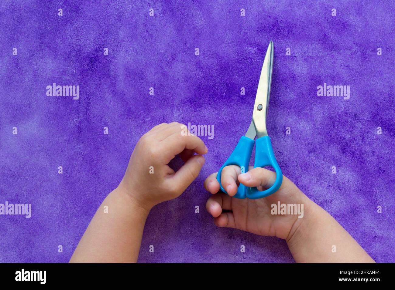Scissors in child hands on the purple background Stock Photo - Alamy
