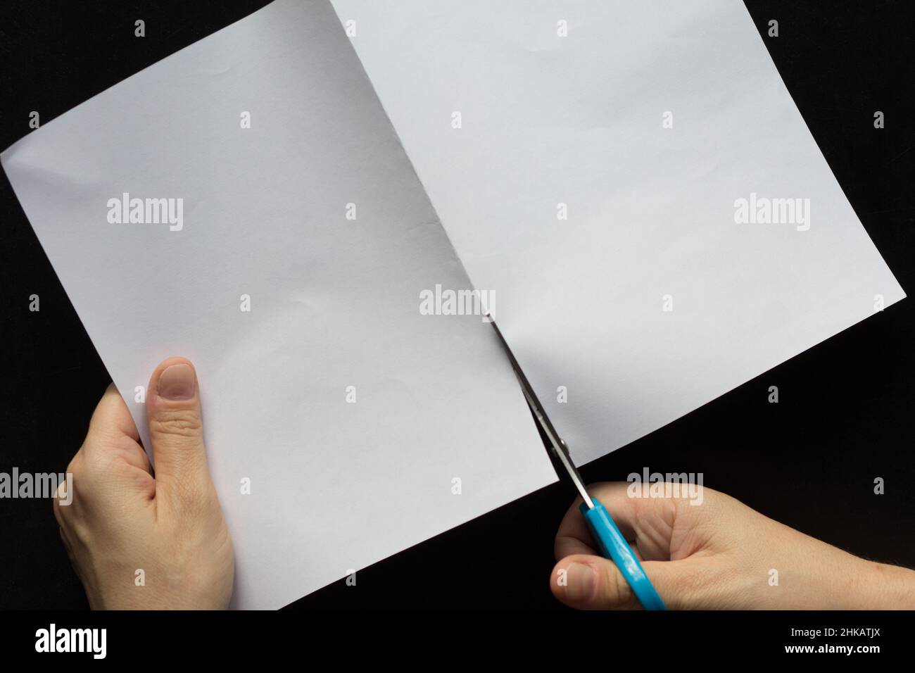 Woman hands cutting rectangular sheet of paper in half on black ...