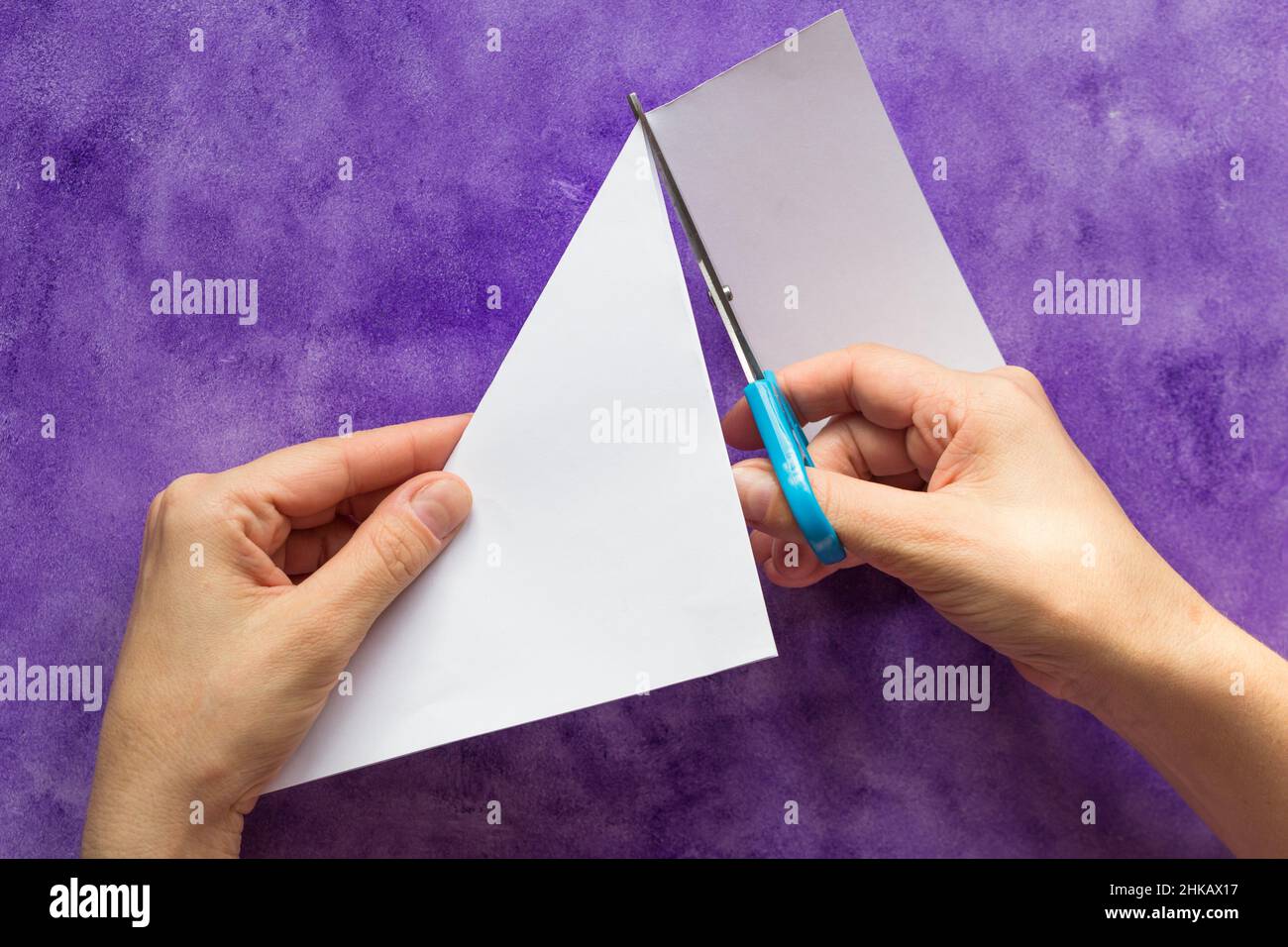 Cutting away edge of sheet of paper with scissors folded corner to make ...
