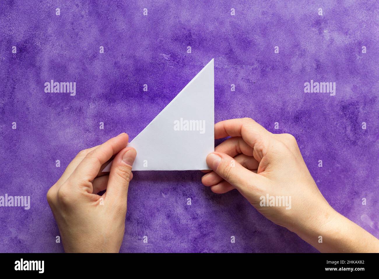 Woman hands holding made folded paper triangle on violet surface Stock ...