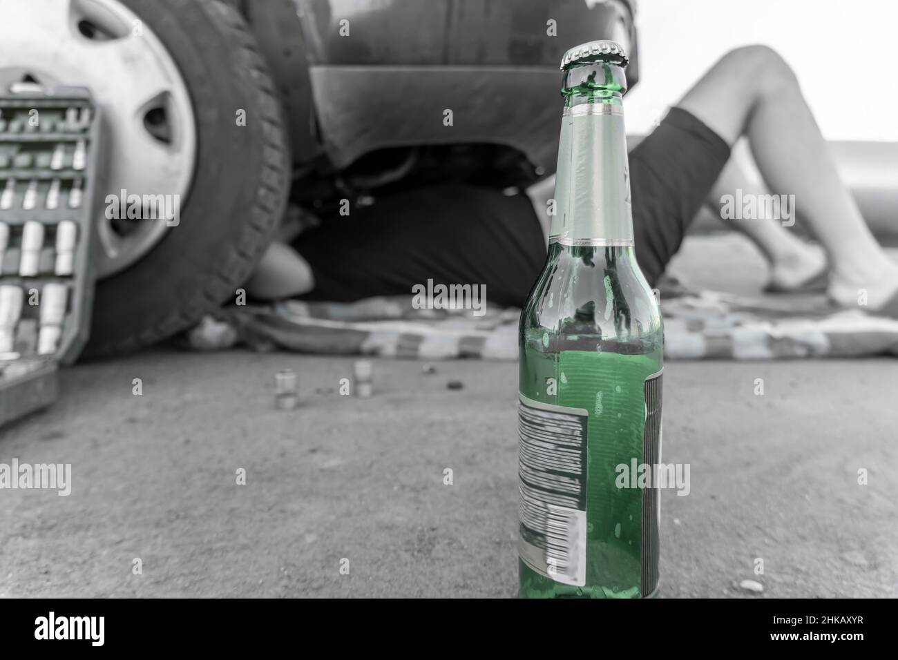 Alcohol and Car repairs.A drunk person lies under the car repairing it ...