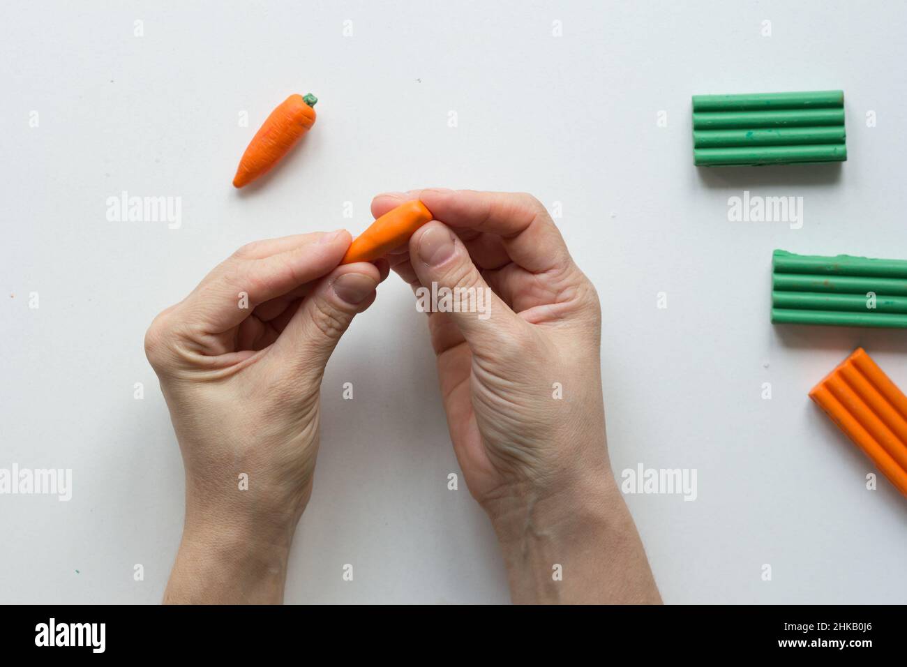 Woman hands making small carrot polymer clay on the white background ...