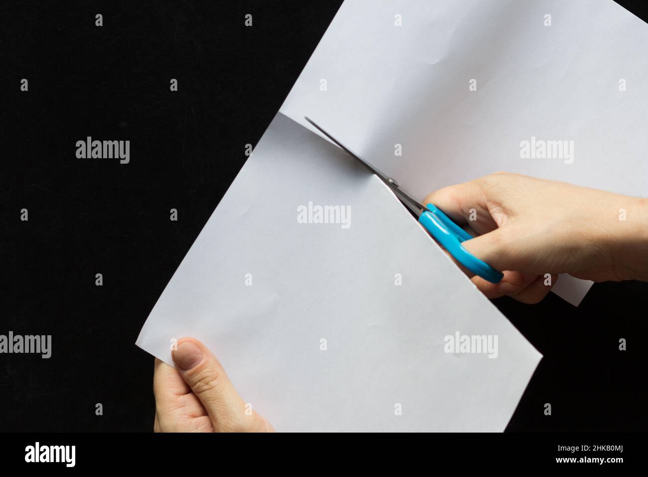 Woman hands cutting rectangular sheet of paper in half on black ...