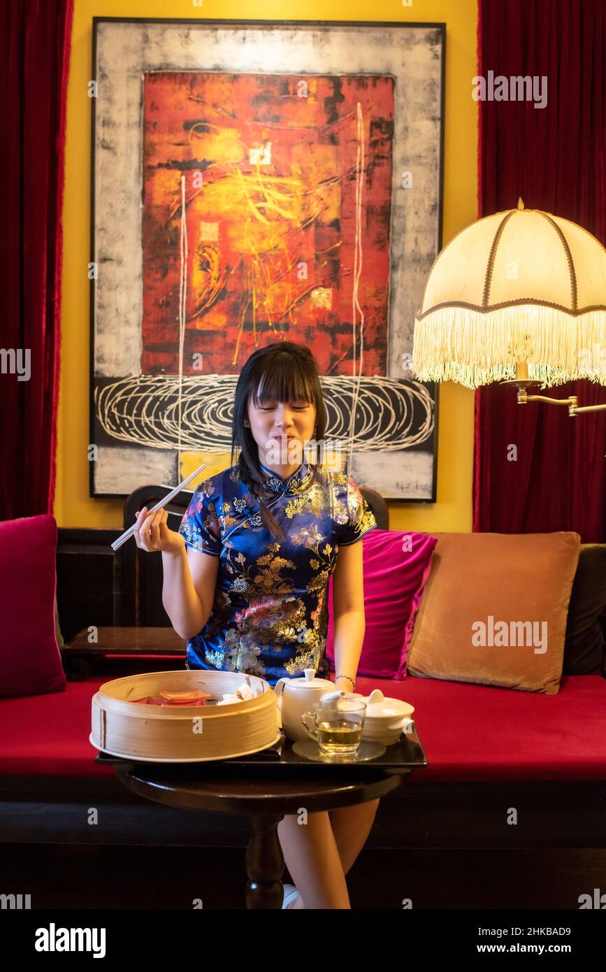 An young Asian Girl is eating Dim Sum in a Chinese dress in front of a ...