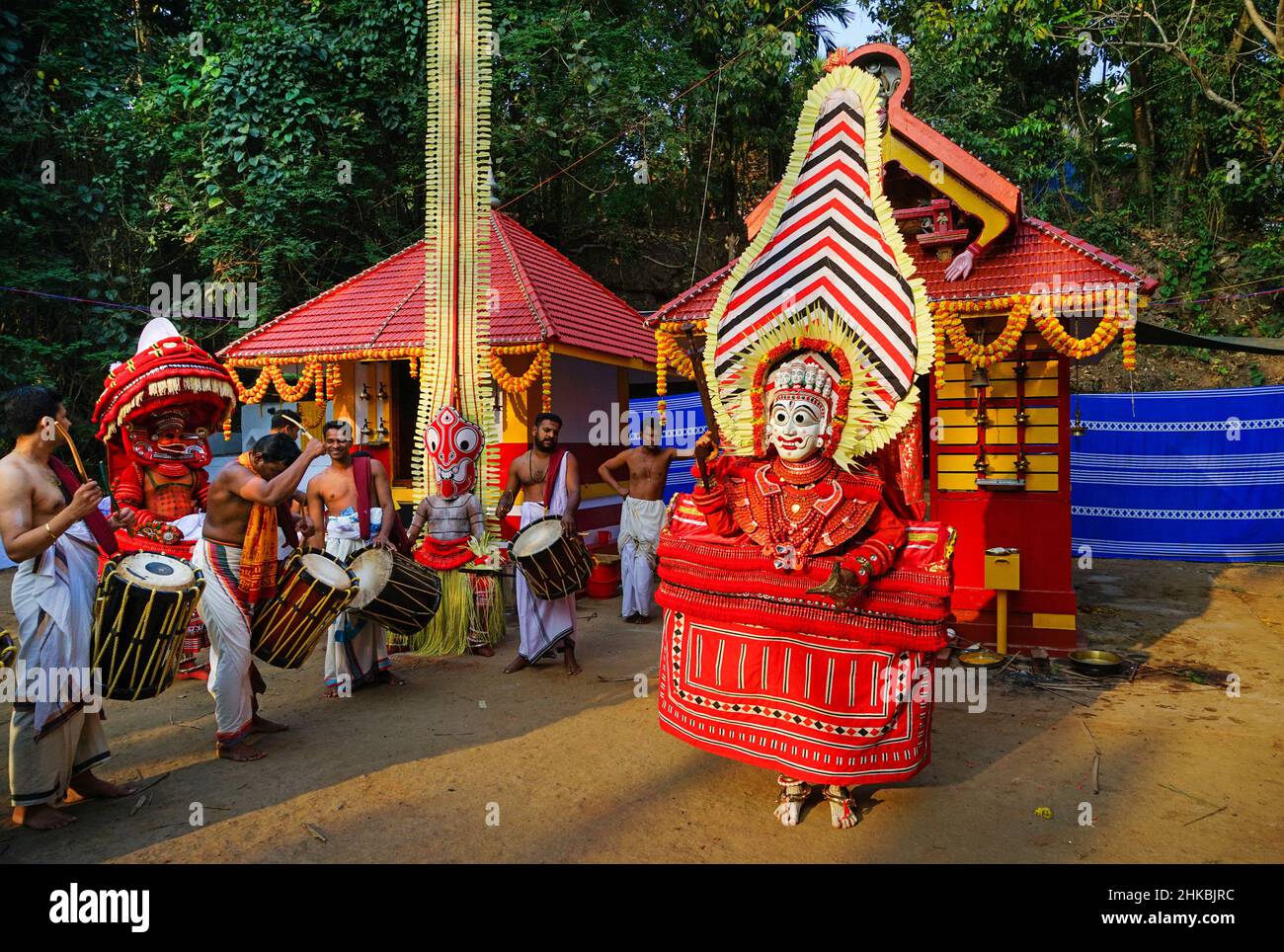 A Theyyam artist is adorned with traditional colorful costume and a ...