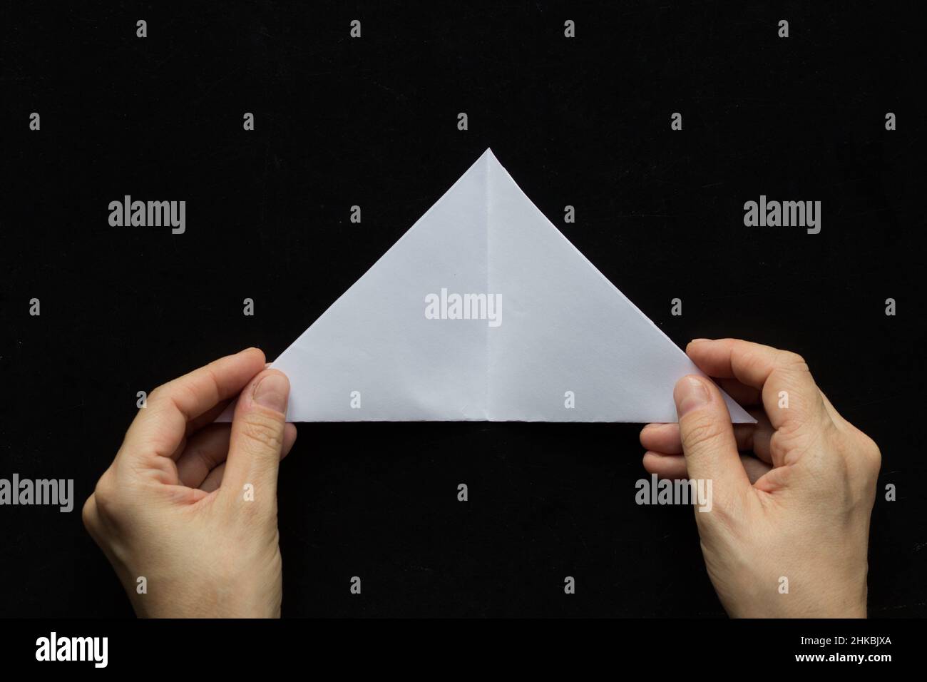 Making snowflake. Step 3. Woman hands holding paper unfolded triangle ...
