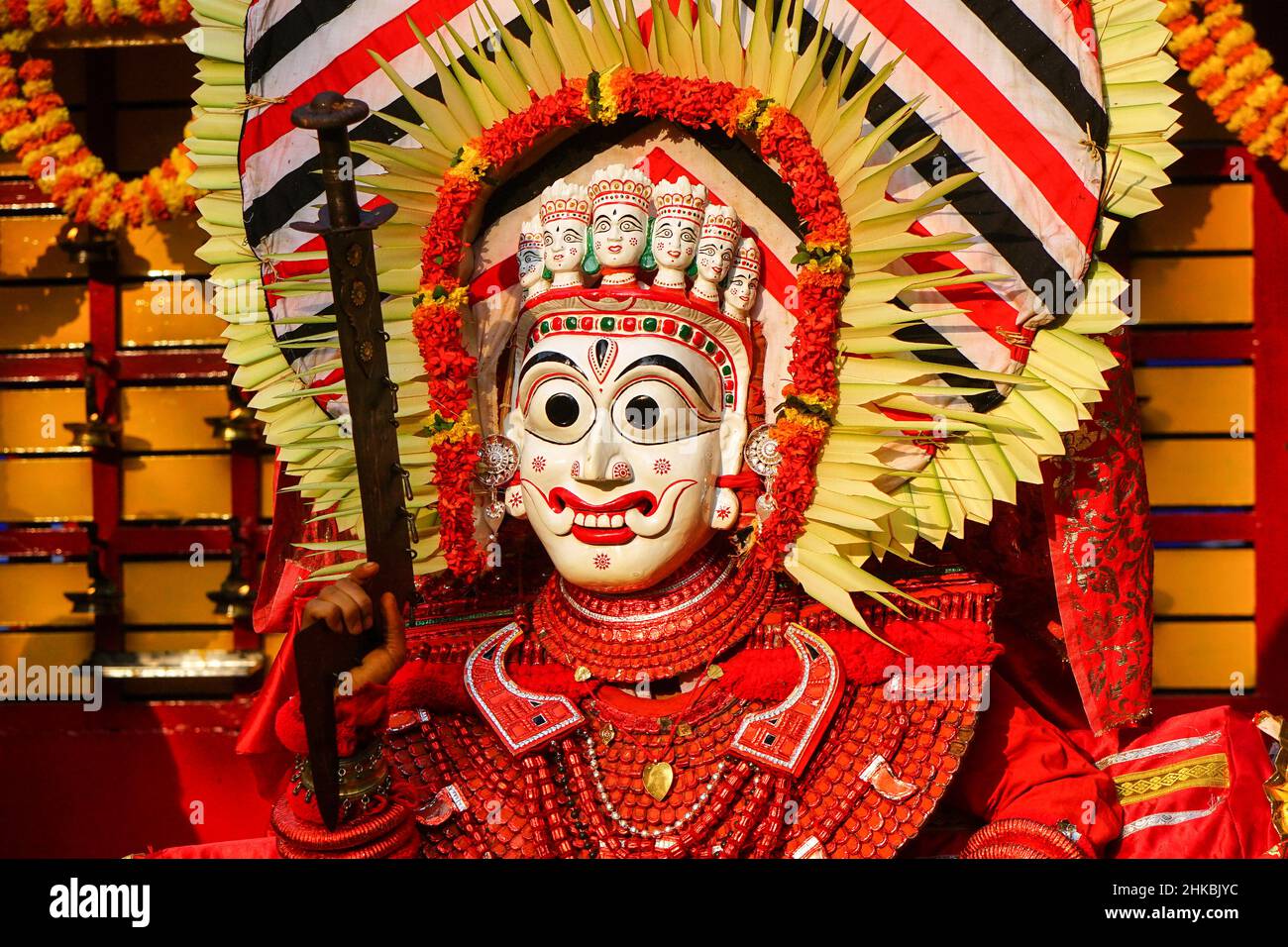 A Theyyam artist is adorned with traditional colorful costume and a ...