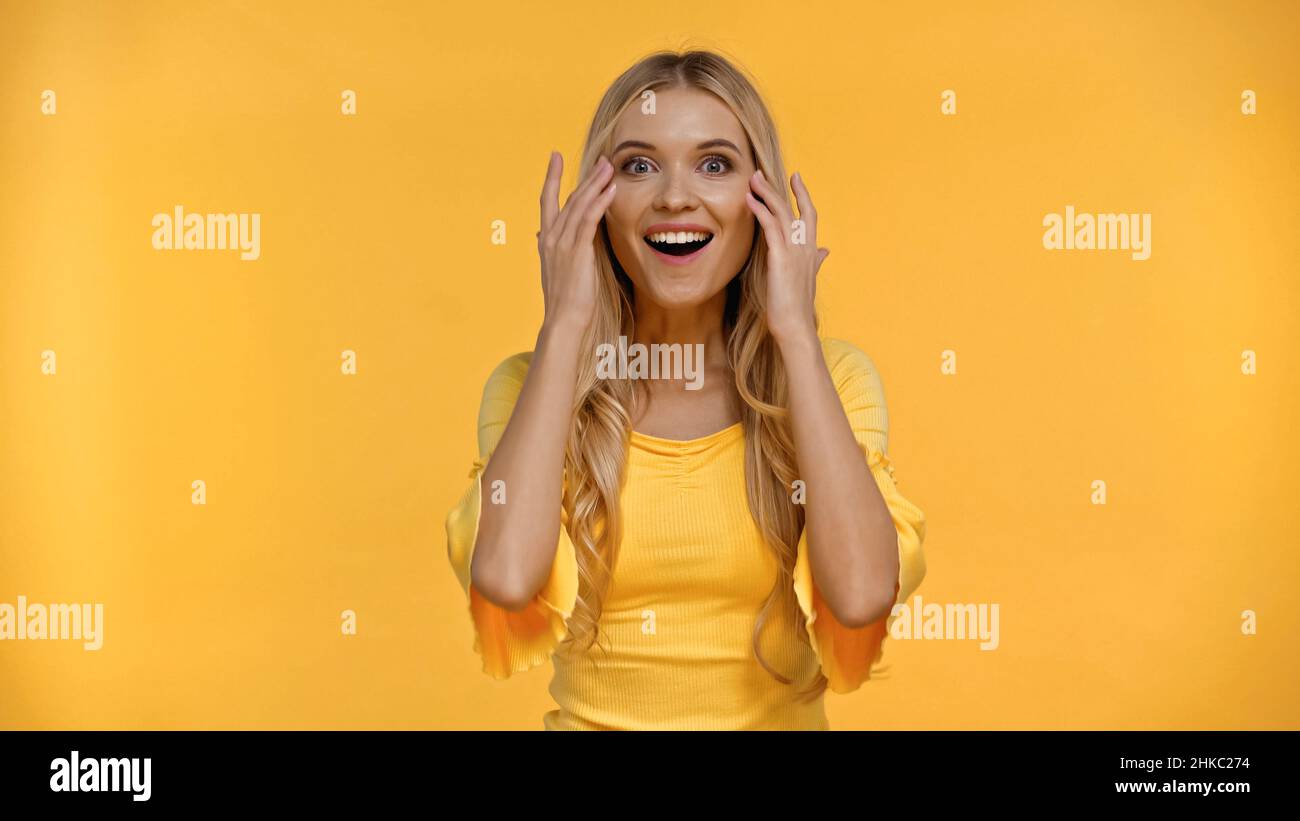 Amazed blonde woman touching face isolated on yellow Stock Photo - Alamy