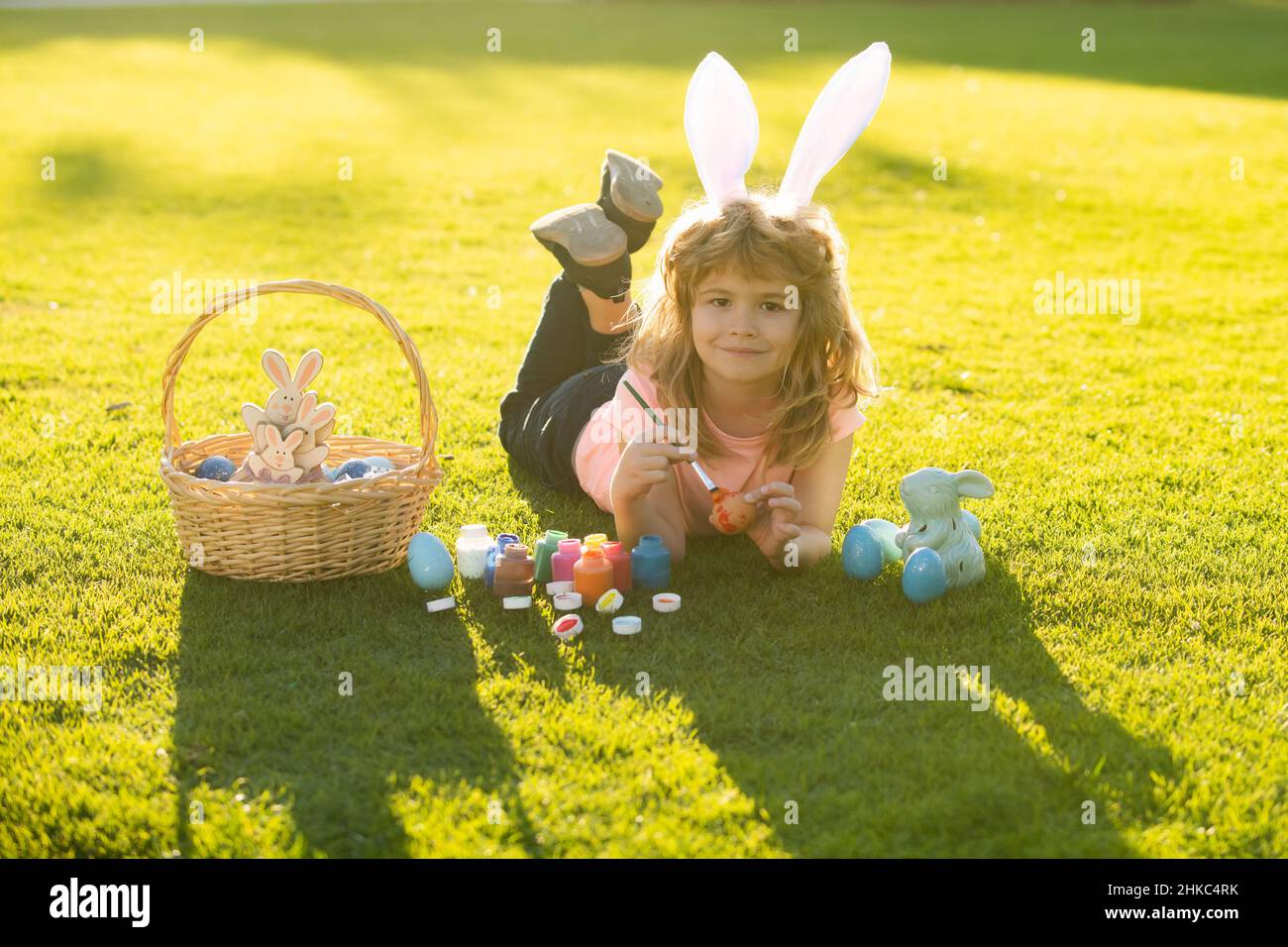 Child boy with easter eggs and bunny ears painting eggs outdoor. Cute ...
