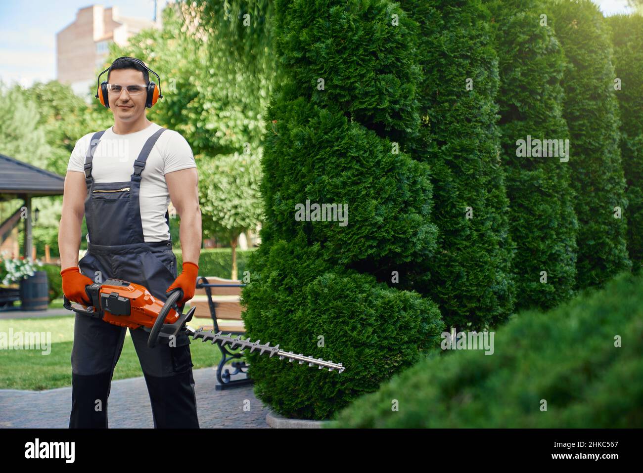Professional male gardener wearing brown overalls, gloves and glasses ...