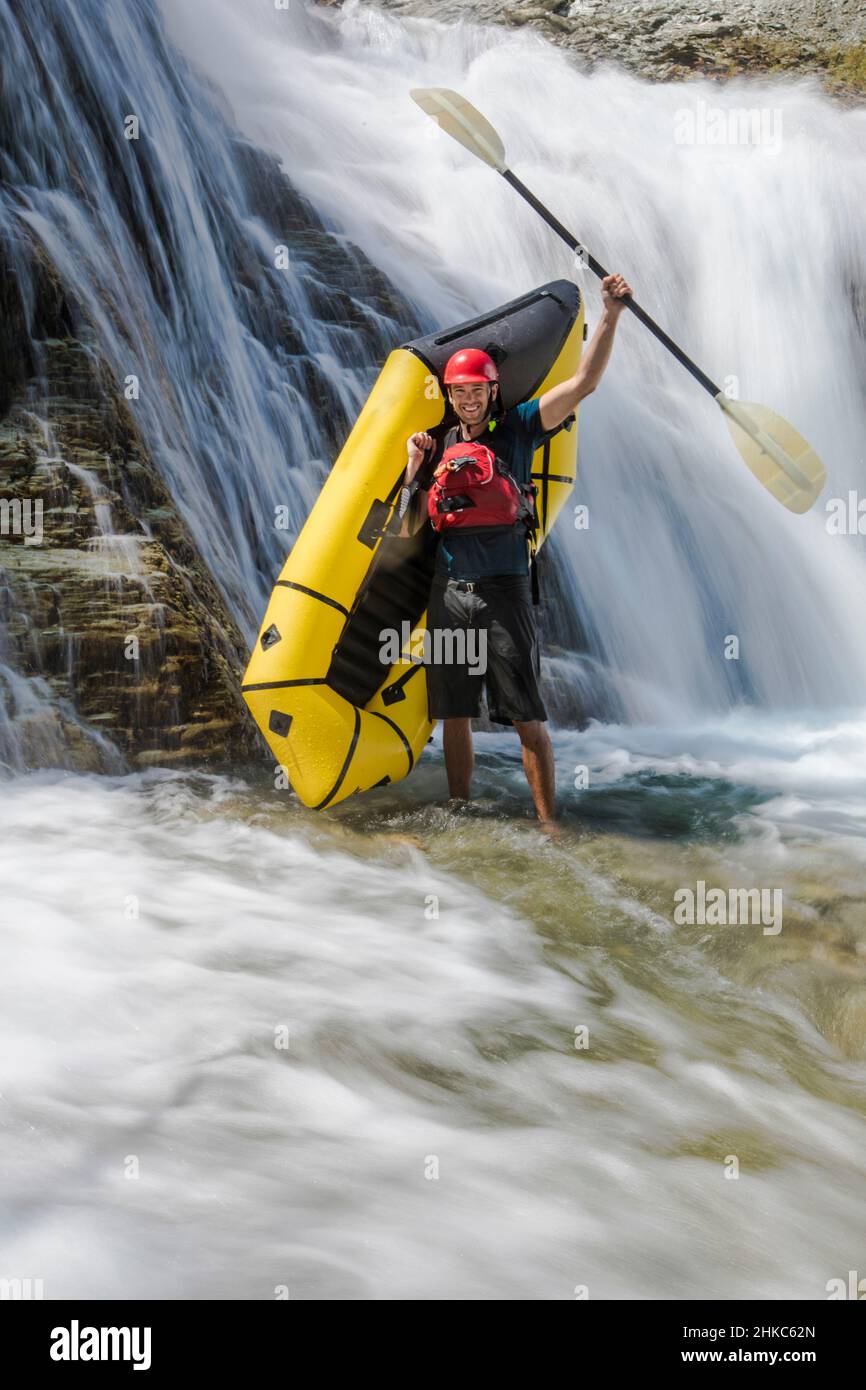 Paddler stands beside waterfall, raising paddle in the air Stock Photo ...