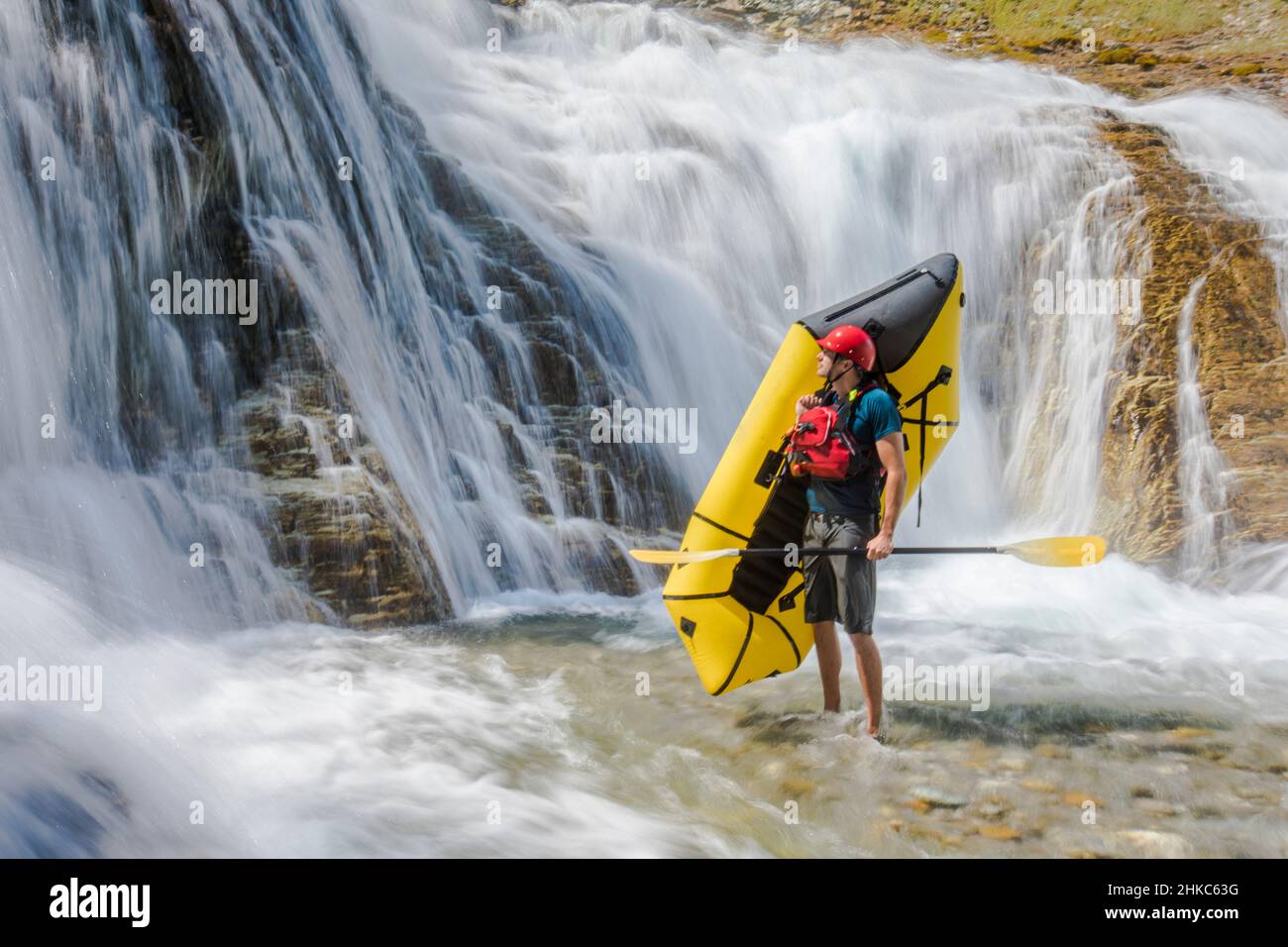 Paddler stands holding raft (packraft) below large waterfall Stock ...