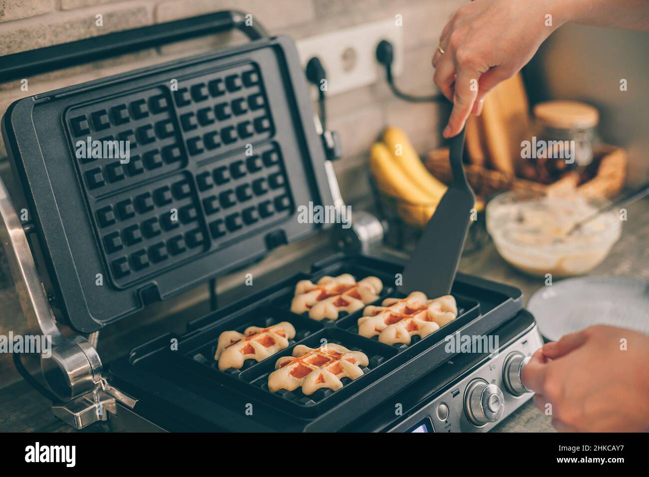 Young woman preparing Belgian waffles in the kitchen. Cooking process ...